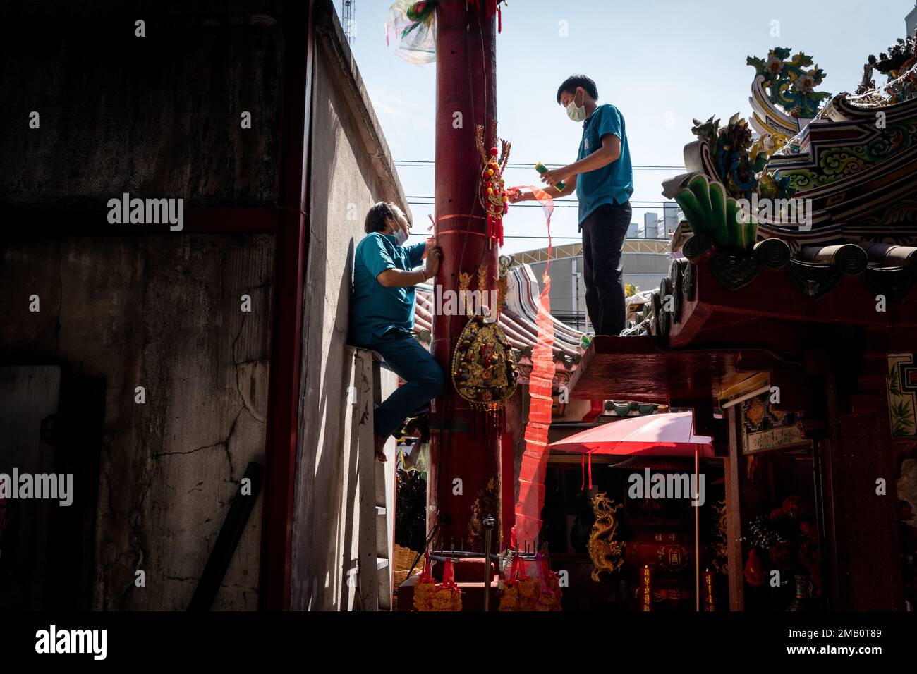 Temple workers wrap colorful fabric around a pillar at a temple in ...