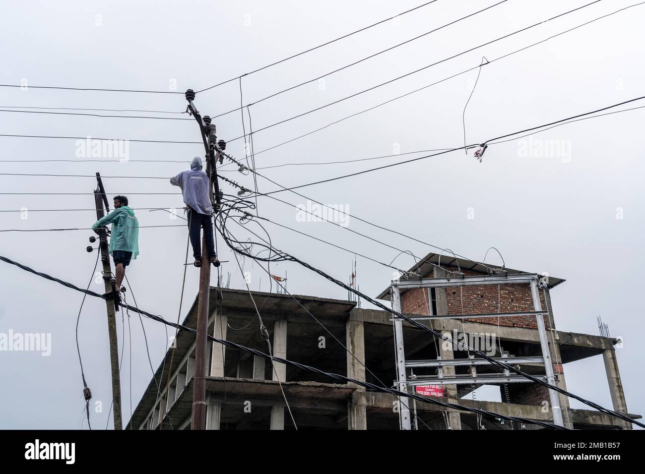 Technicians wearing raincoats work on high electricity poles under rain ...