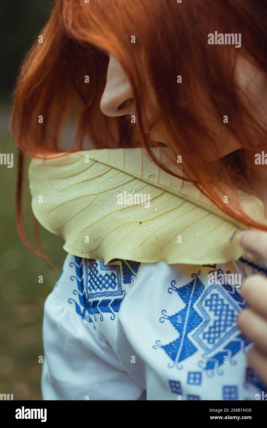 Close up ginger haired woman looking at dew drops on leaf portrait ...