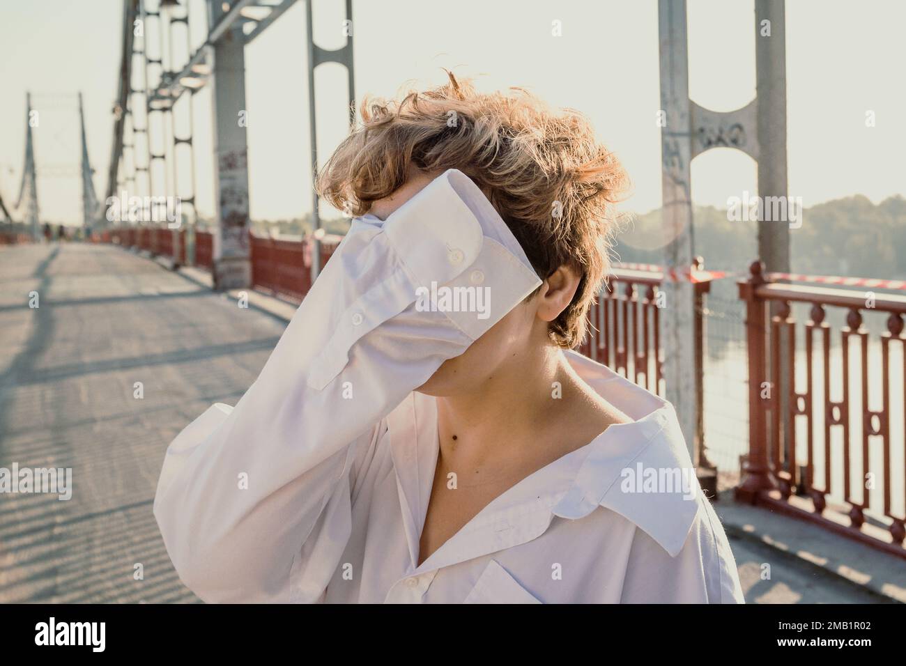 Close up woman hiding face behind shirt sleeve standing on bridge ...