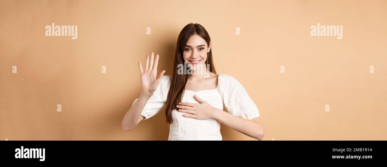 Cute smiling girl make promise, put hand on heart and tell truth, being ...