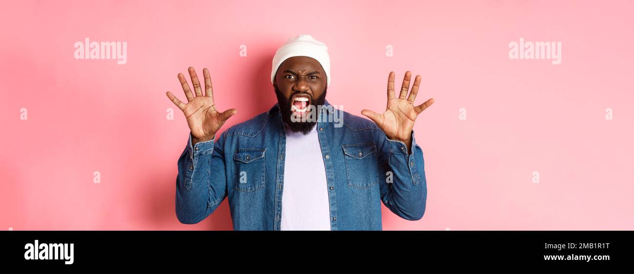 Angry african-american guy in beanie, scare you, roaring and screaming ...