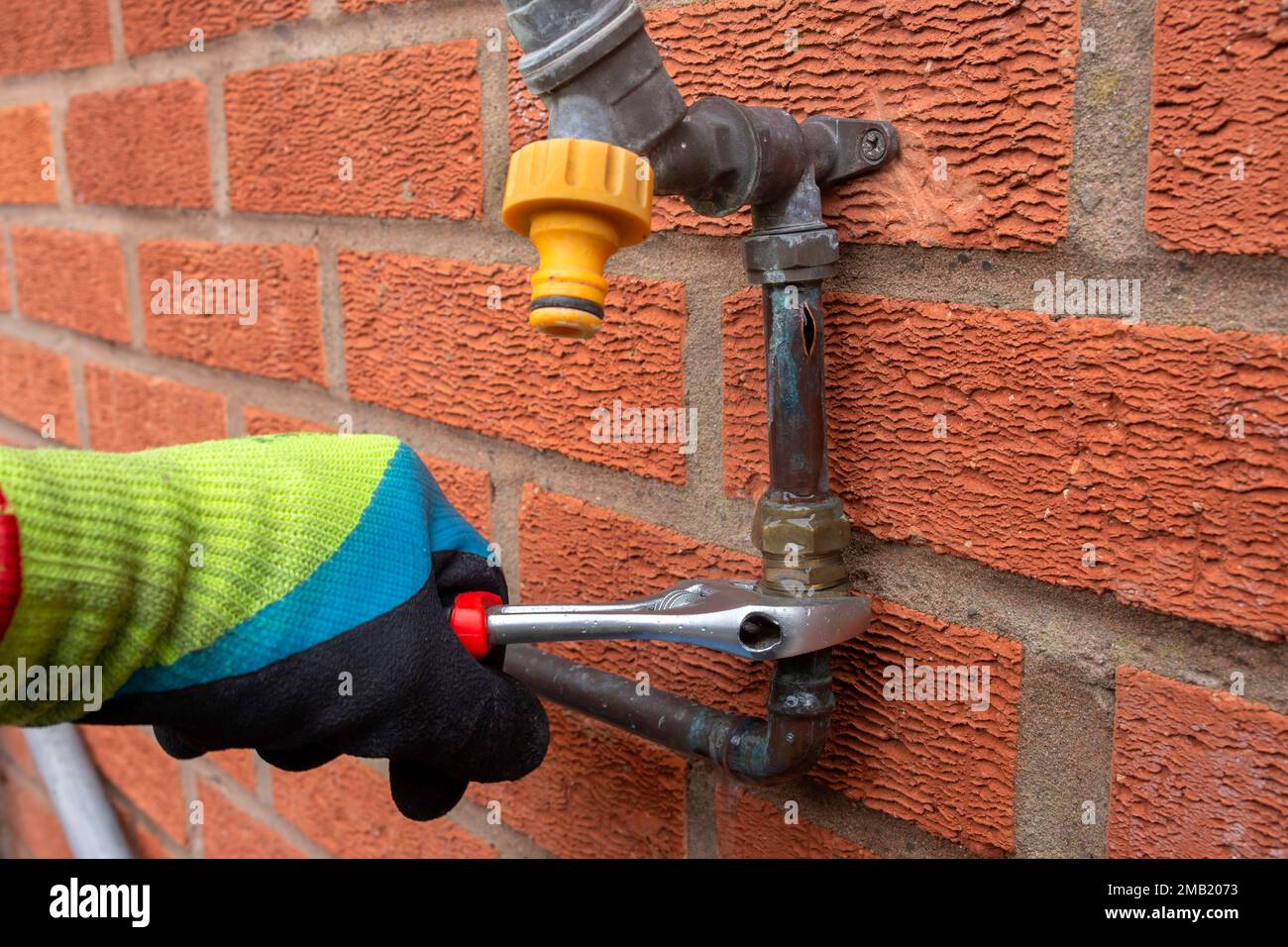 Man replacing burst copper water pipe outdoors. Unscrewing a brass ...