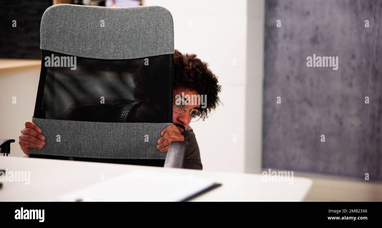Scared Man Hiding Behind Office Desk In Room Stock Photo - Alamy