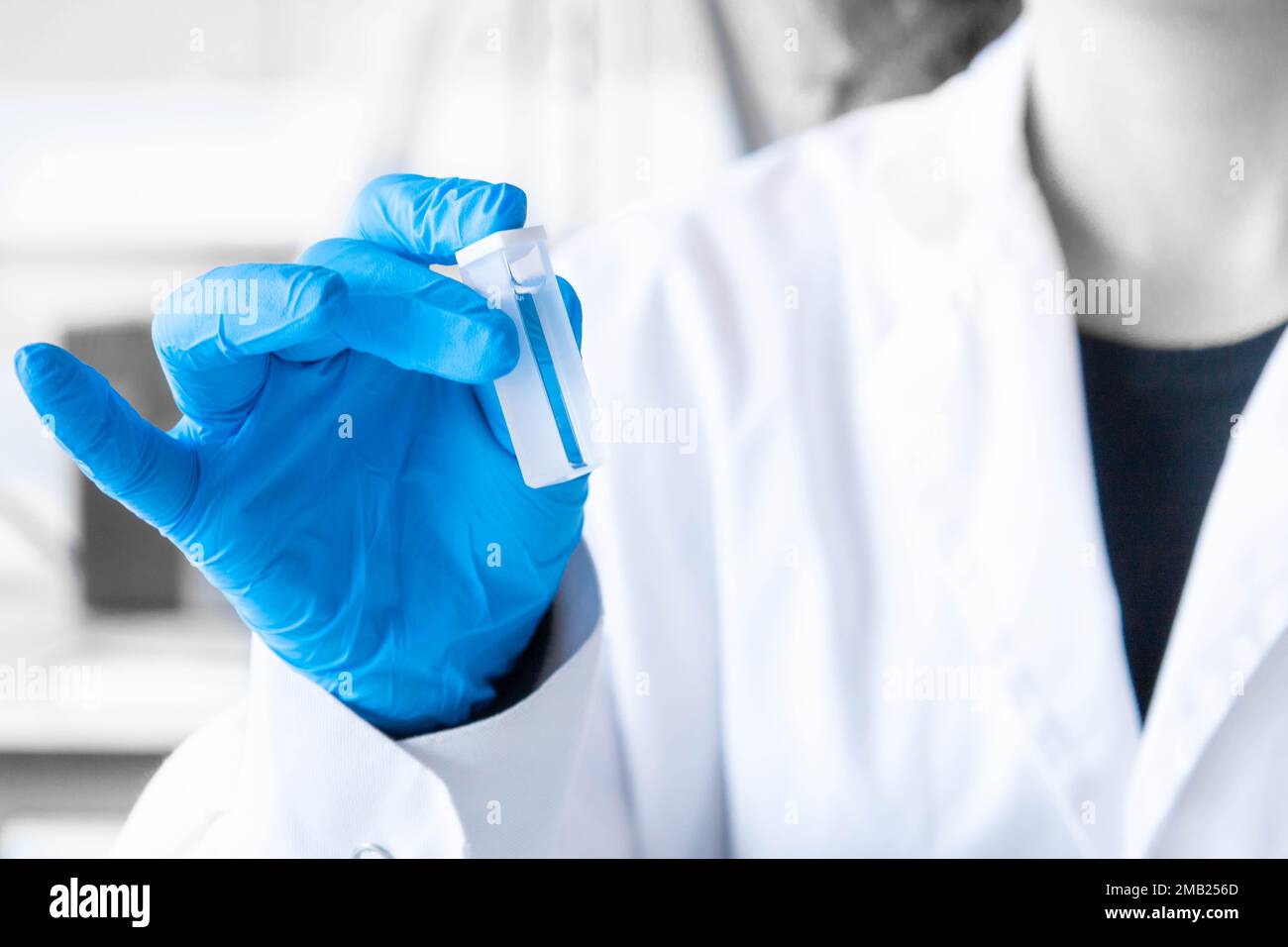 Close up scientist hand holding a spectrophotometry cuvette with blue ...