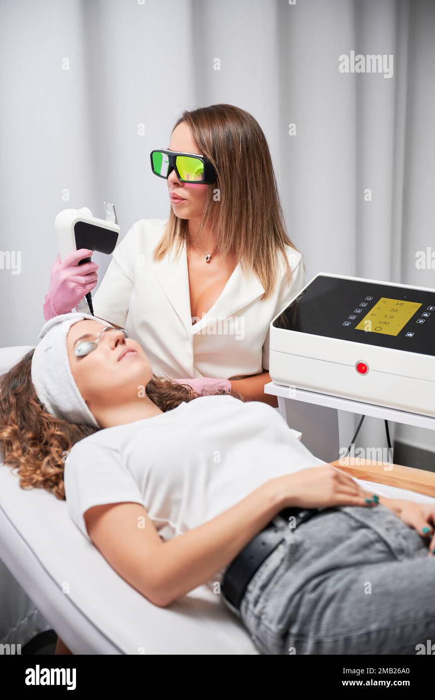 Beautician in protective glasess examining working element of laser ...