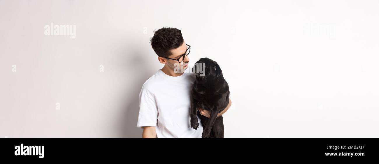 Handsome young man holding his black pug, dot and pet owner looking ...