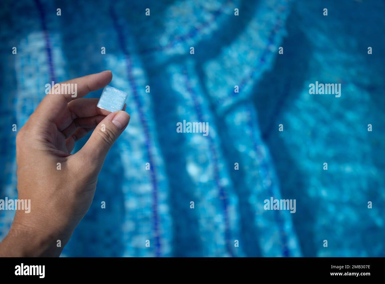Hand holding small tile from floor of swimming pool. Design of the ...