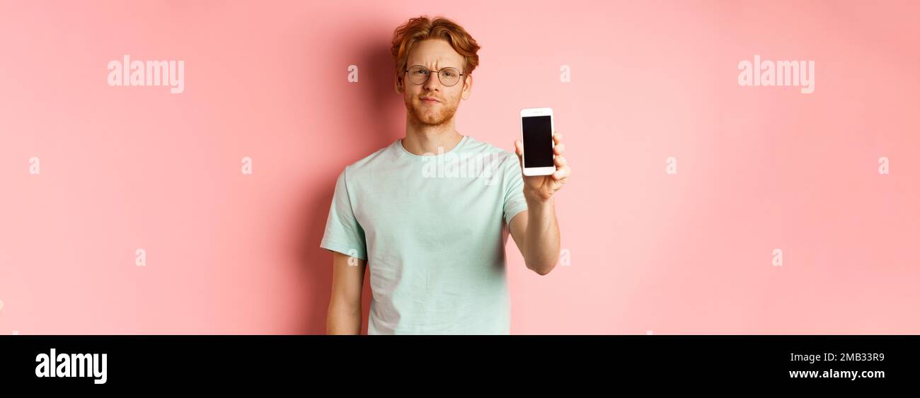 Disappointed male model frowning, showing smartphone screen, standing ...
