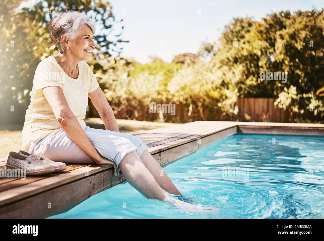 Happy elderly woman with her feet in the pool while on a vacation ...
