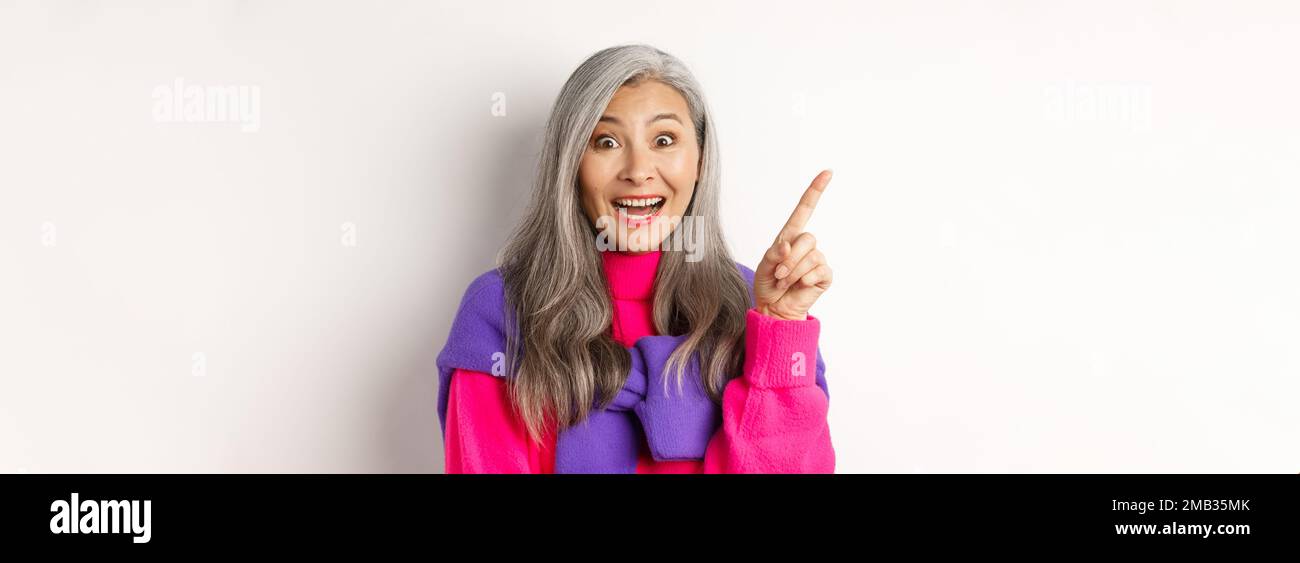 Close up of beautiful asian female model pointing finger at upper left ...