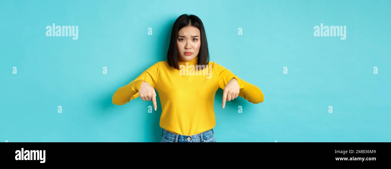 Shopping concept. Sad and worried asian girl frowning silly, pointing ...