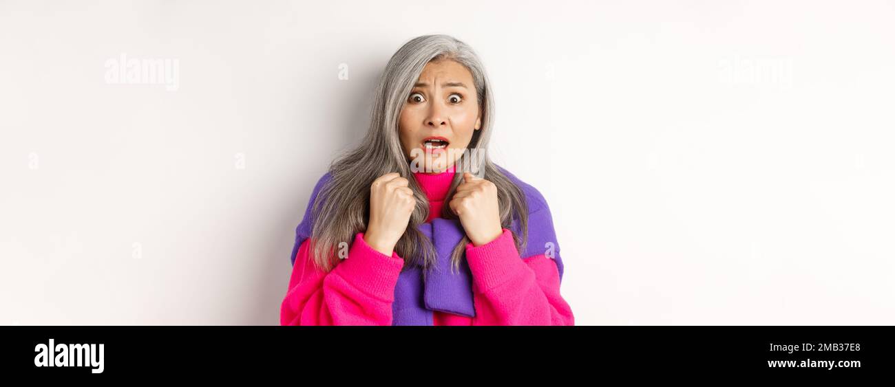 Close up of scared asian senior woman gasping, looking frightened and ...