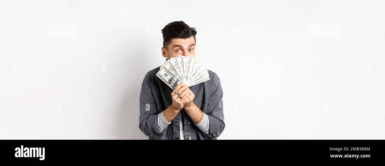 Excited funny guy hiding face behind dollar bills and smiling, showing ...