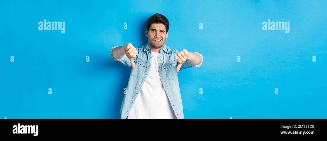 Disappointed man showing thumbs down and grimacing at something awful ...