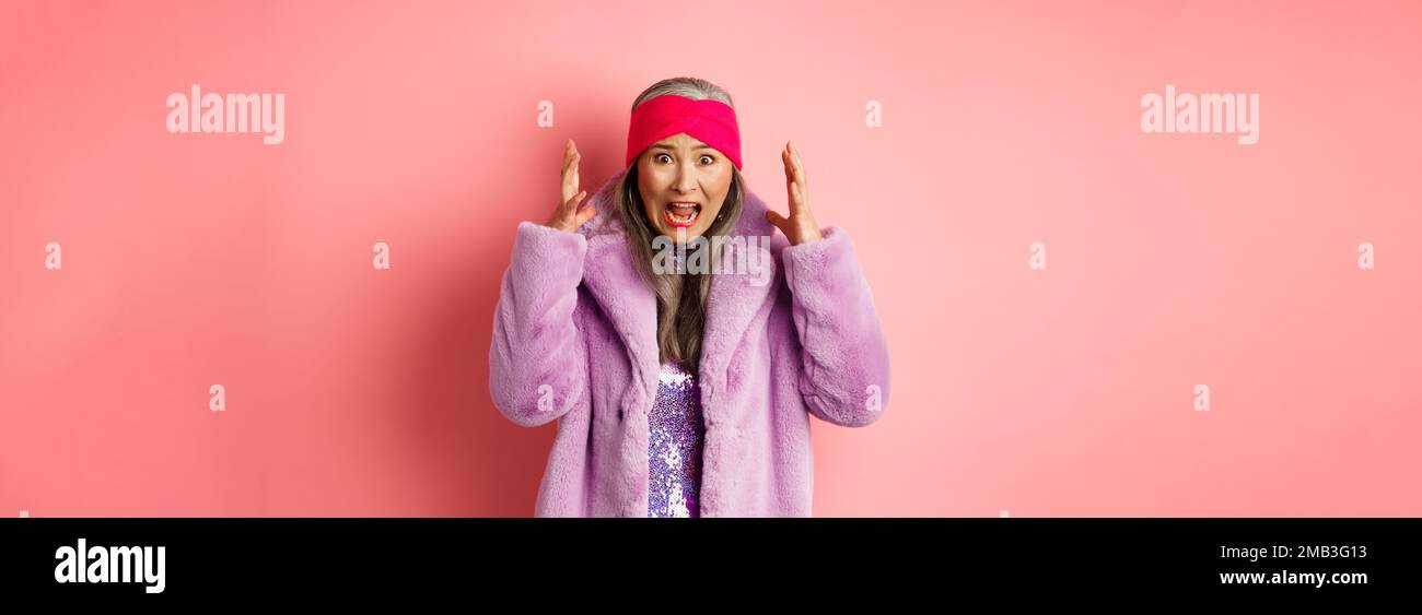 Anxious asian senior woman in stylish faux fur coat screaming, shaking ...