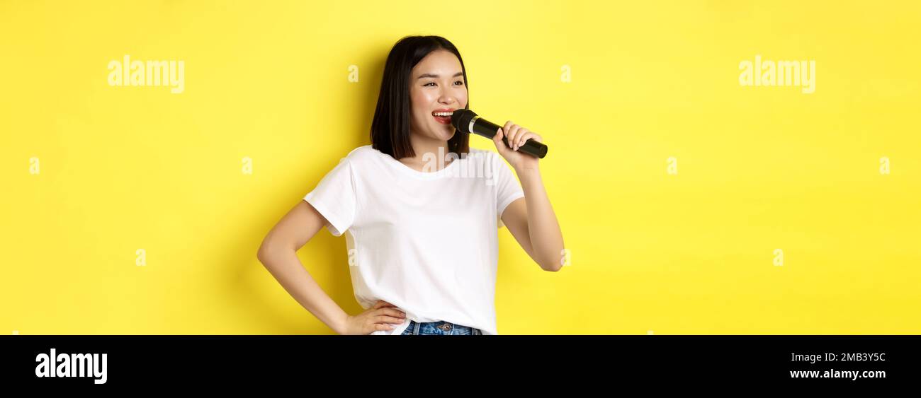 Happy asian woman singing song in karaoke, holding microphone and ...
