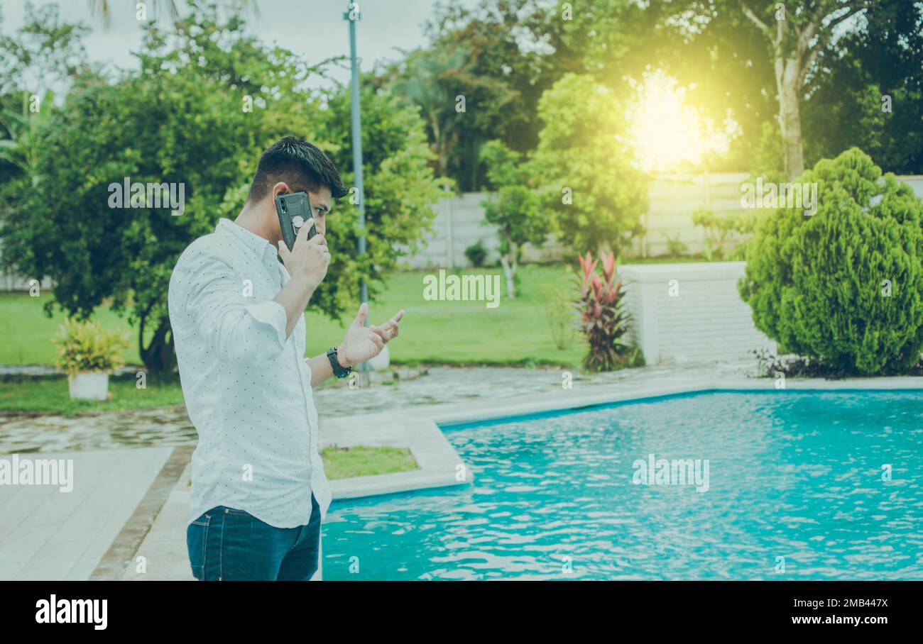 Attractive guy standing talking on the phone near the pool edge ...