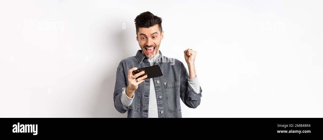 Happy man shouting yes, winning video game on mobile phone and ...
