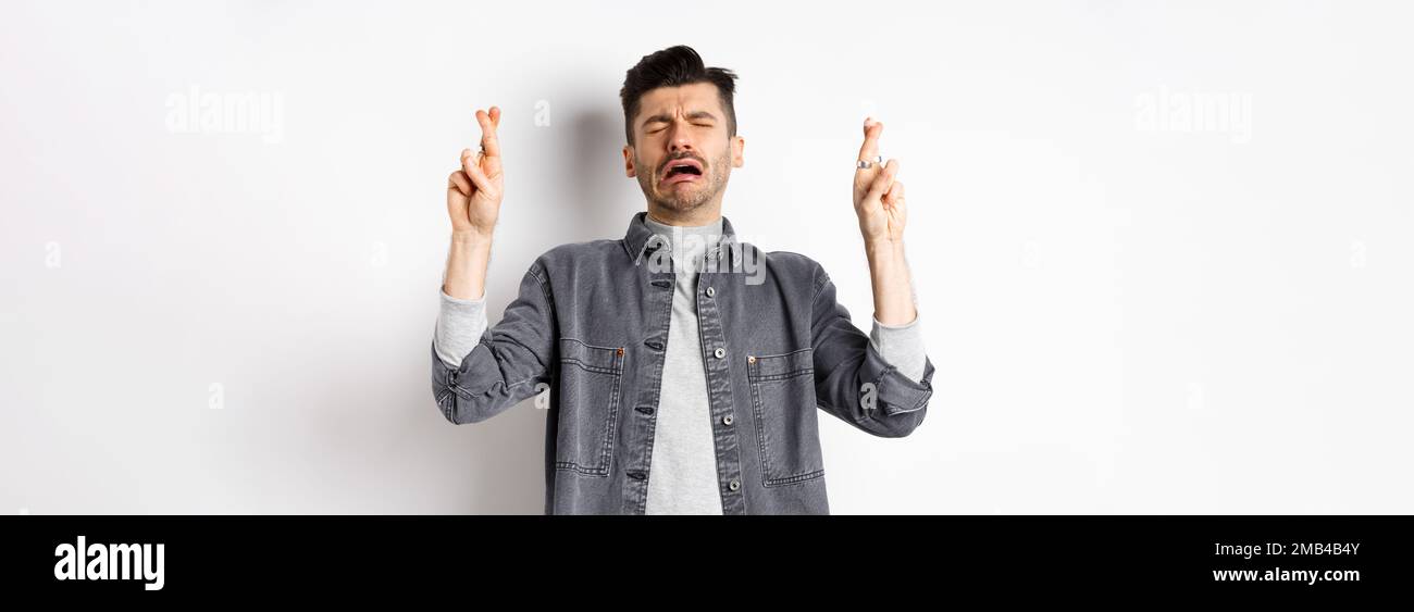 Sad and miserable man hoping god, cross fingers and crying, praying or ...