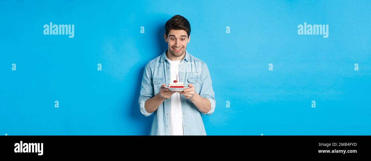 Happy man looking at birthday cake and making with, standing over blue ...