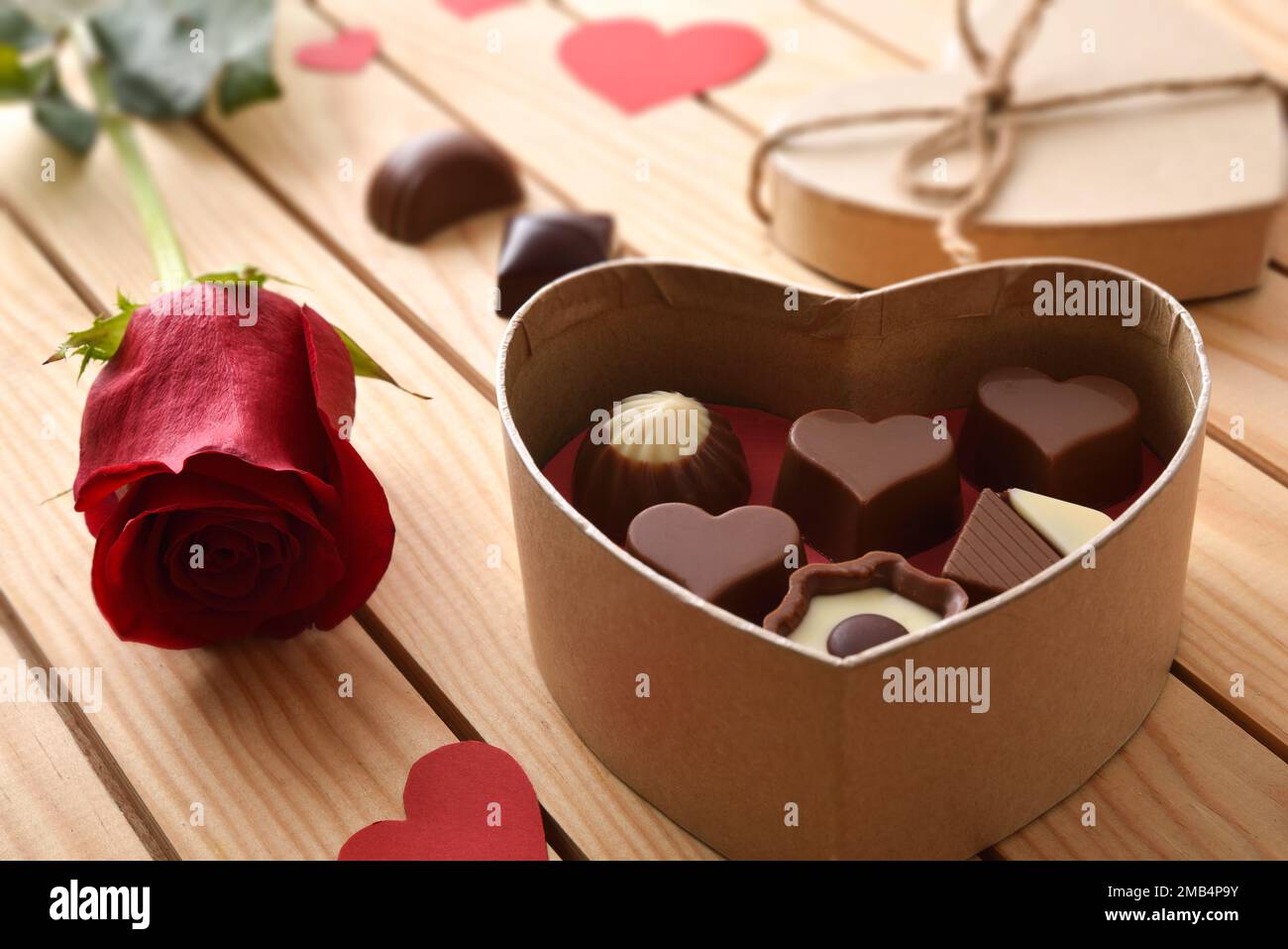 Box with assorted chocolates and red rose on wooden slatted table ...
