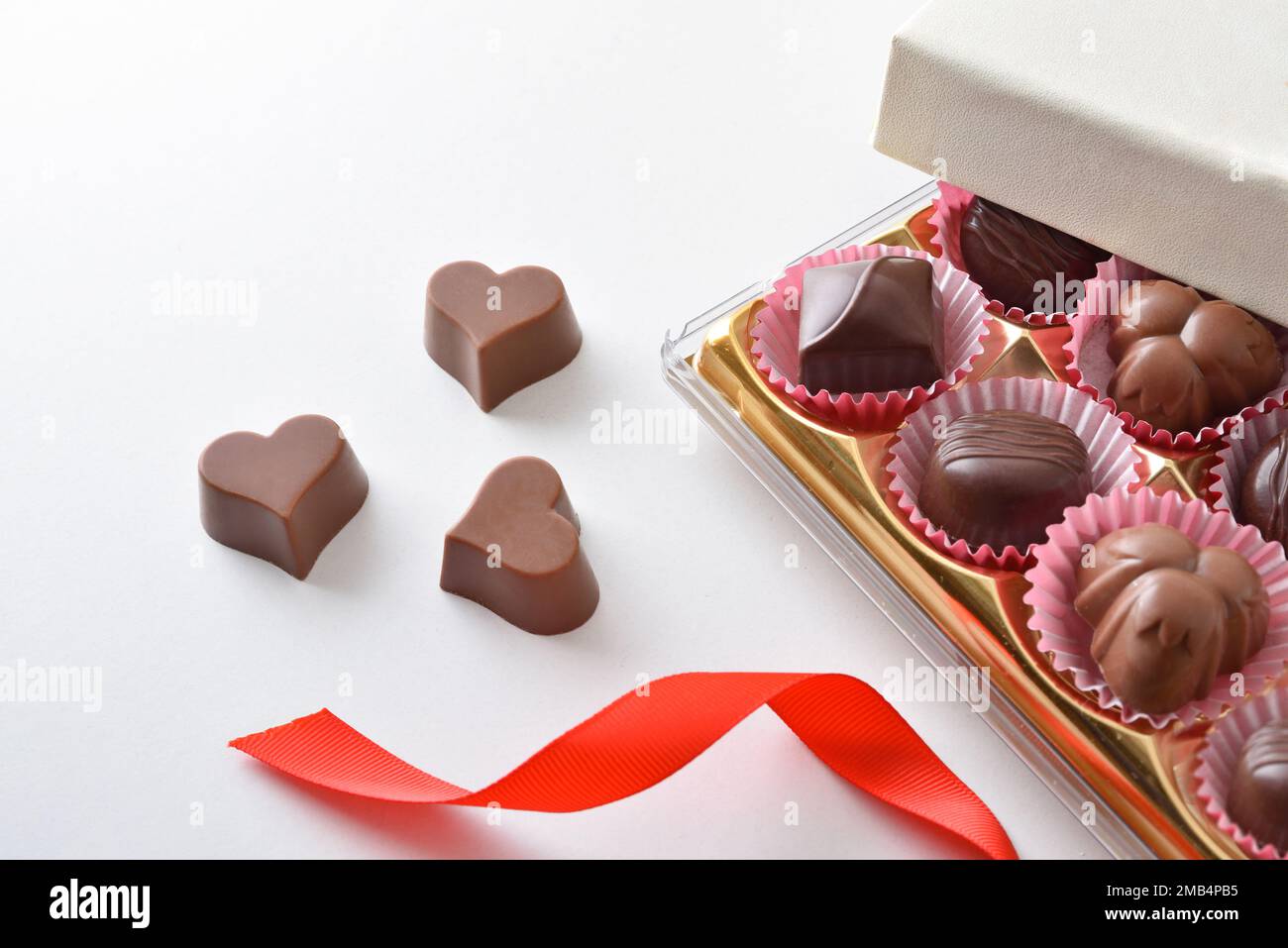 Box with assortment of chocolates on white table for event with red bow ...