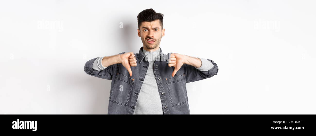 Disappointed guy showing thumbs down and frowning, looking skeptical at ...