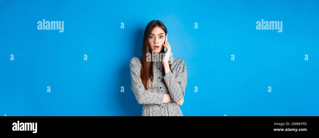 Shocked girl talking on mobile phone, gasping amazed at camera ...