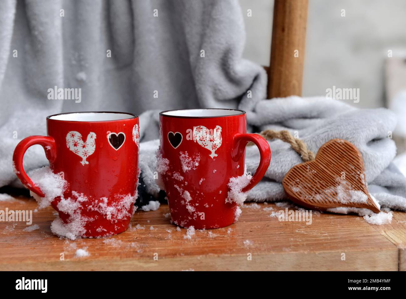 two red mugs with wooden heart shaped on a wooden plank and little bit ...