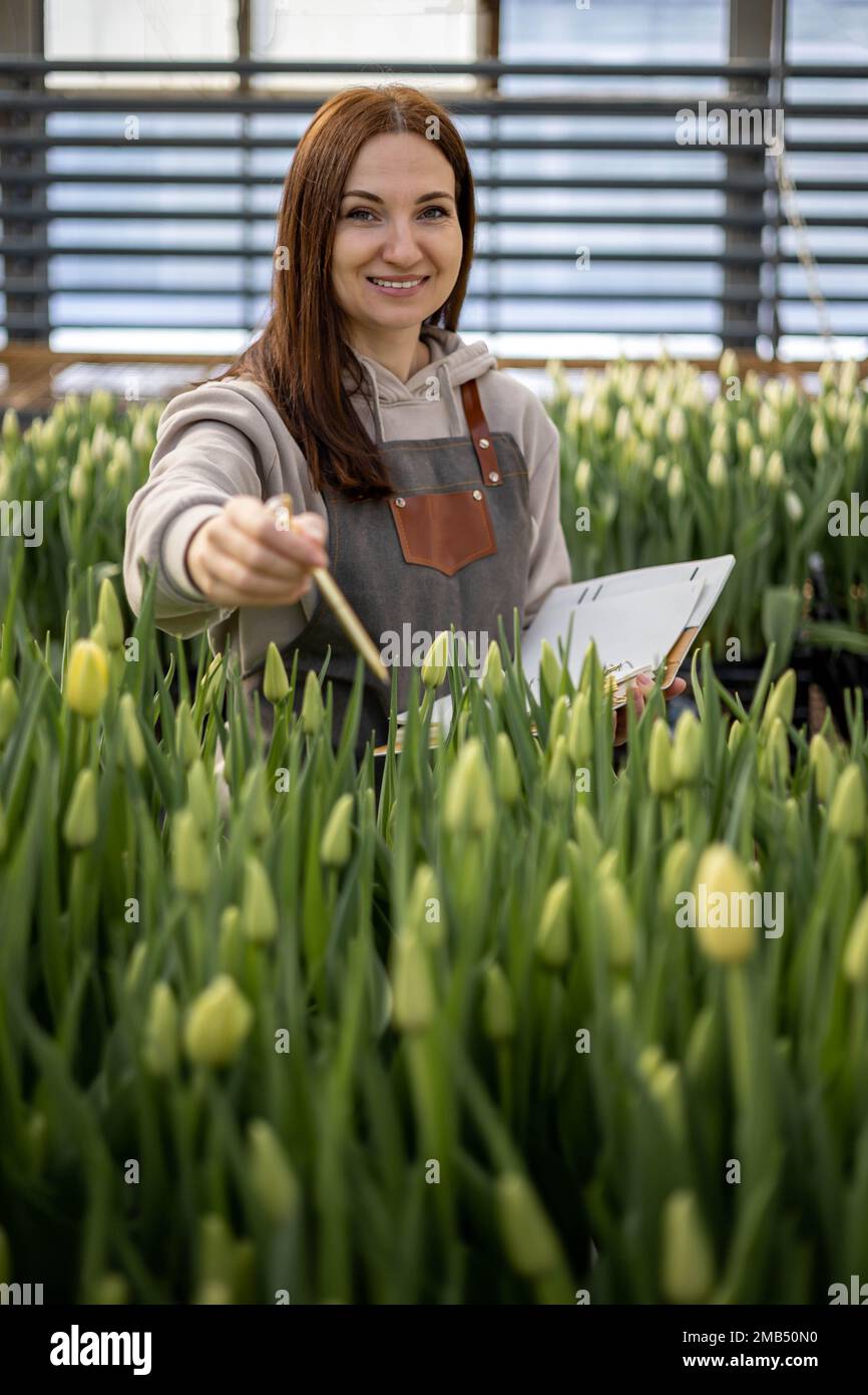 Portrait happy female gardener posing greenhouse surrounded by fresh ...