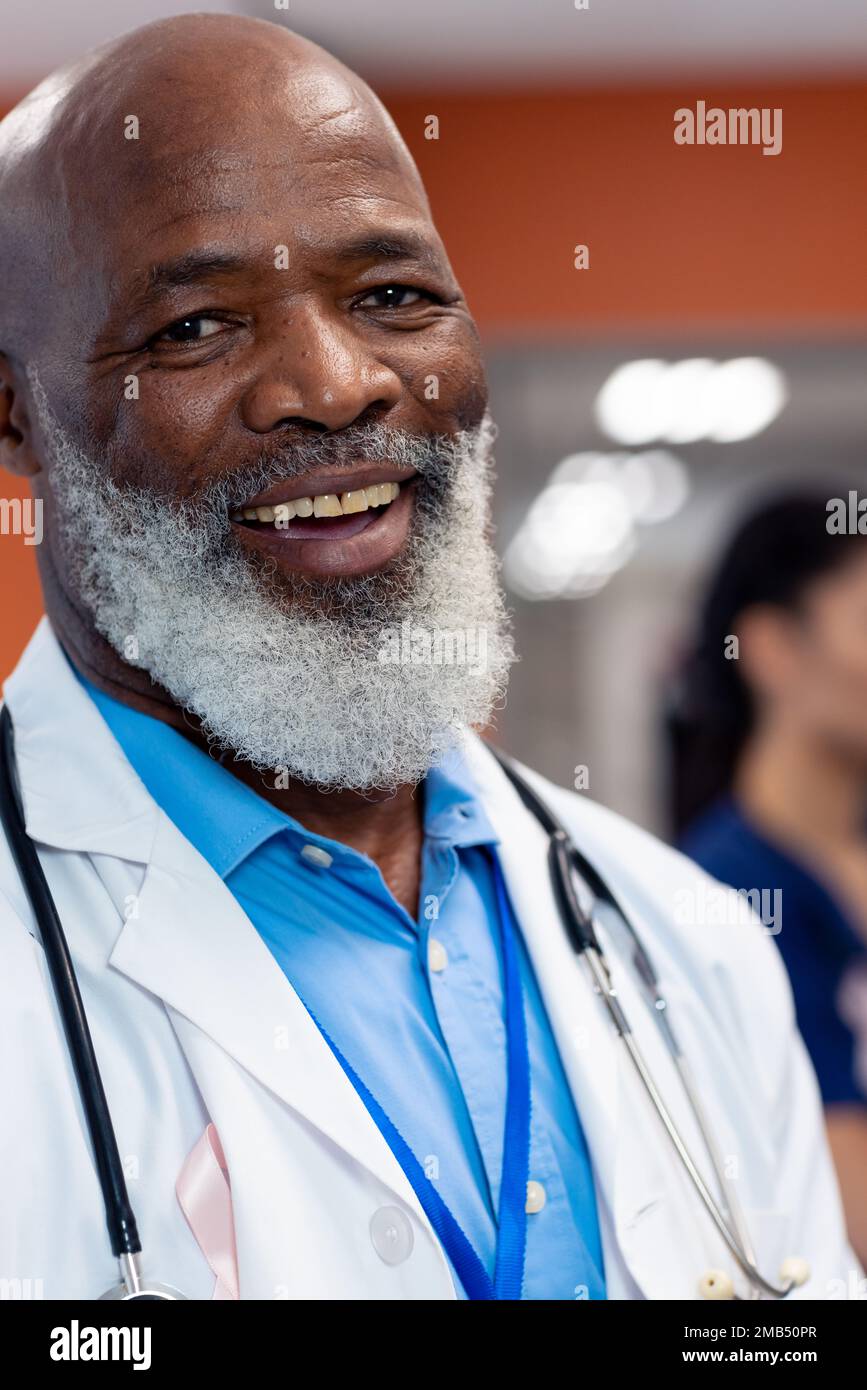 Vertical portrait of smiling senior male doctor with cancer ribbon in ...