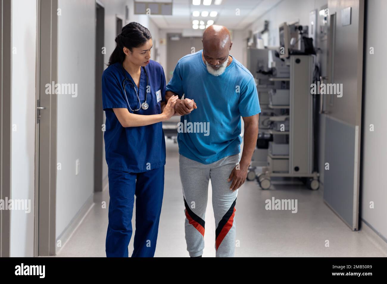 Diverse female doctor helping senior male patient walk in corridor ...