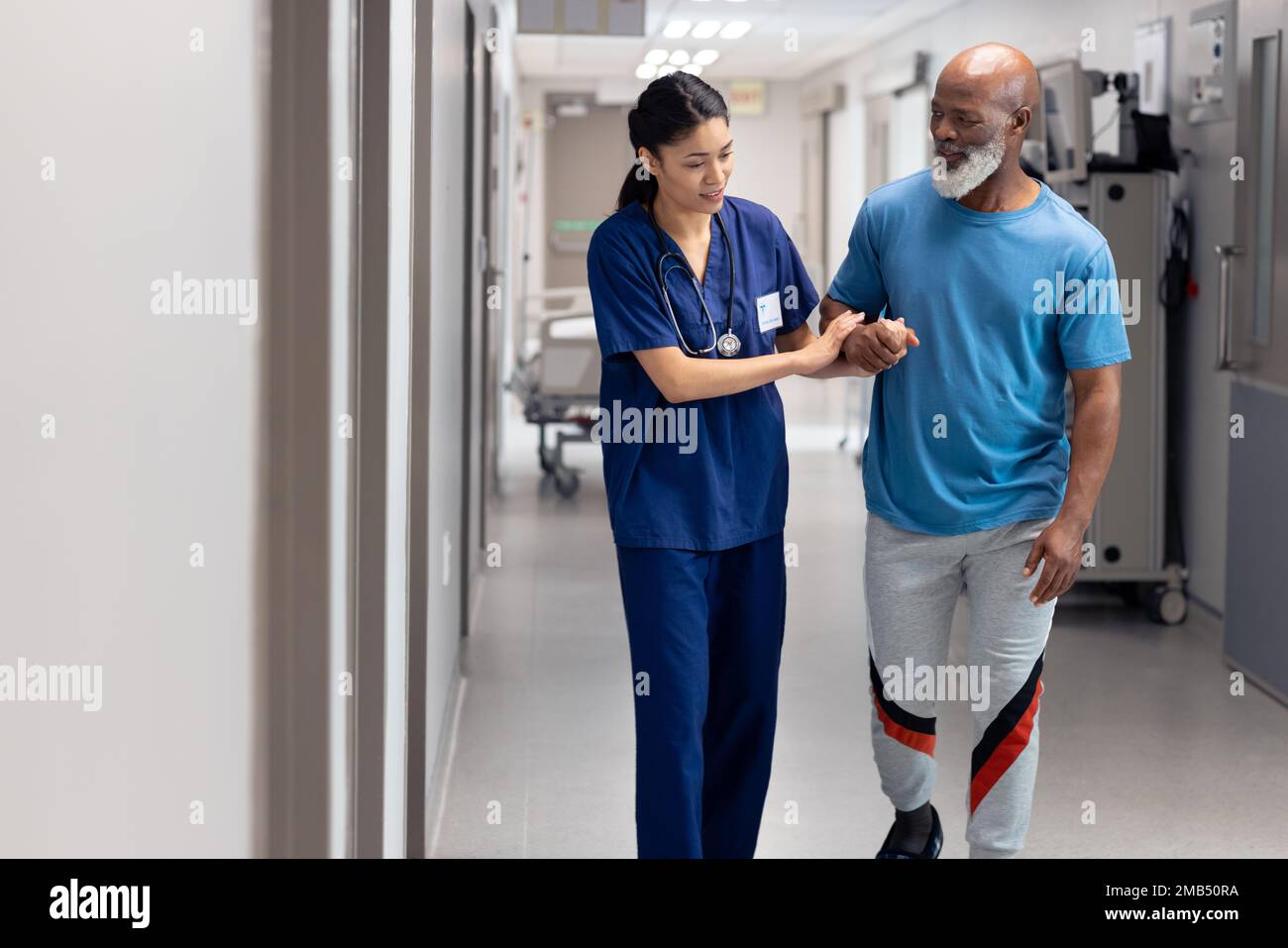 Diverse female doctor helping senior male patient walk in corridor ...