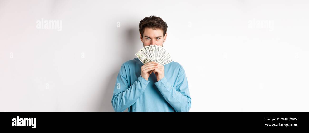 Finance concept. Smiling young man covering face behind money, showing ...