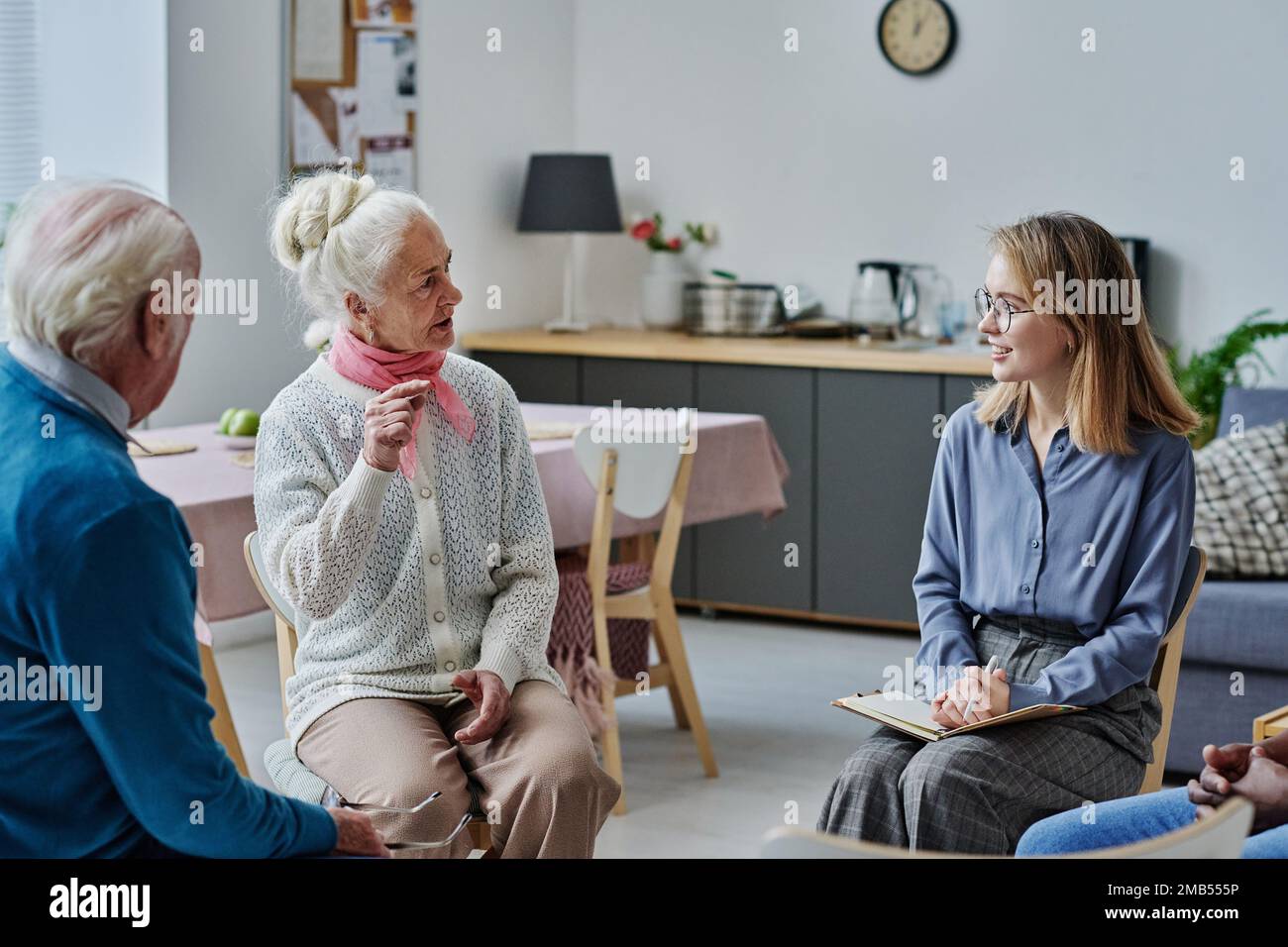 Young woman listening to elder people while they sitting on chairs ...