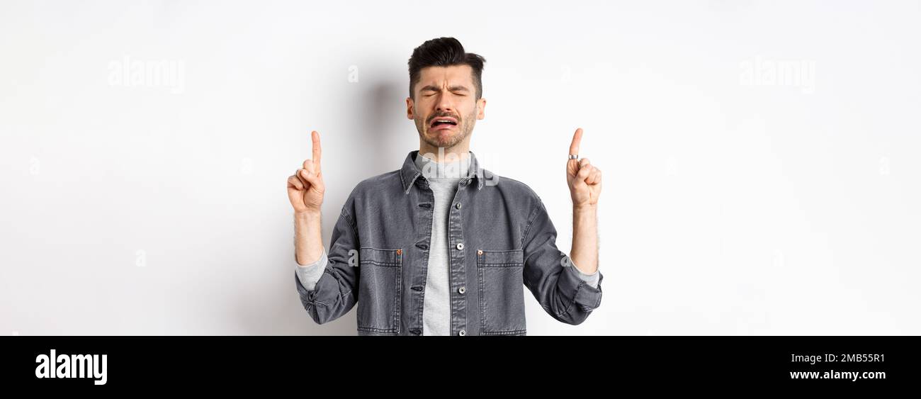 Sad and miserable guy crying while pointing fingers up, showing ...