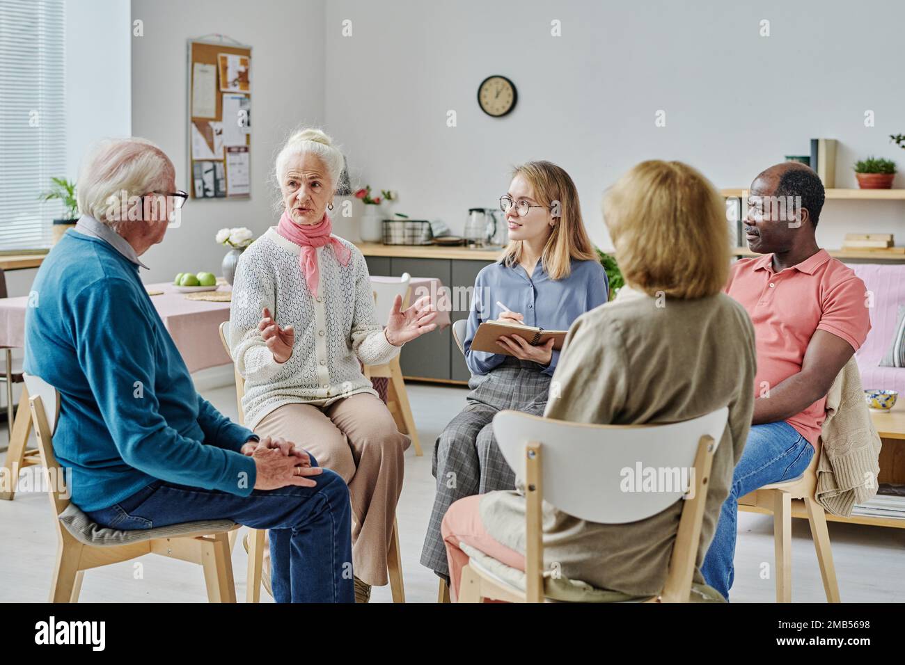 Group of senior people sitting on chairs and talking to each other ...