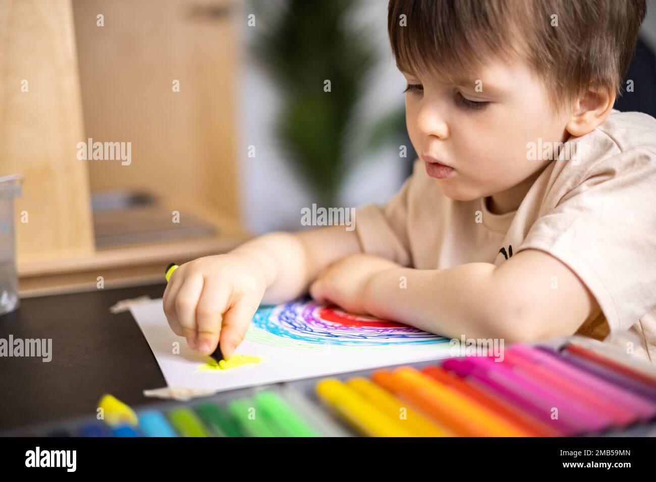 Enthusiastic male kid drawing multicolor rainbow paper sheet closeup ...