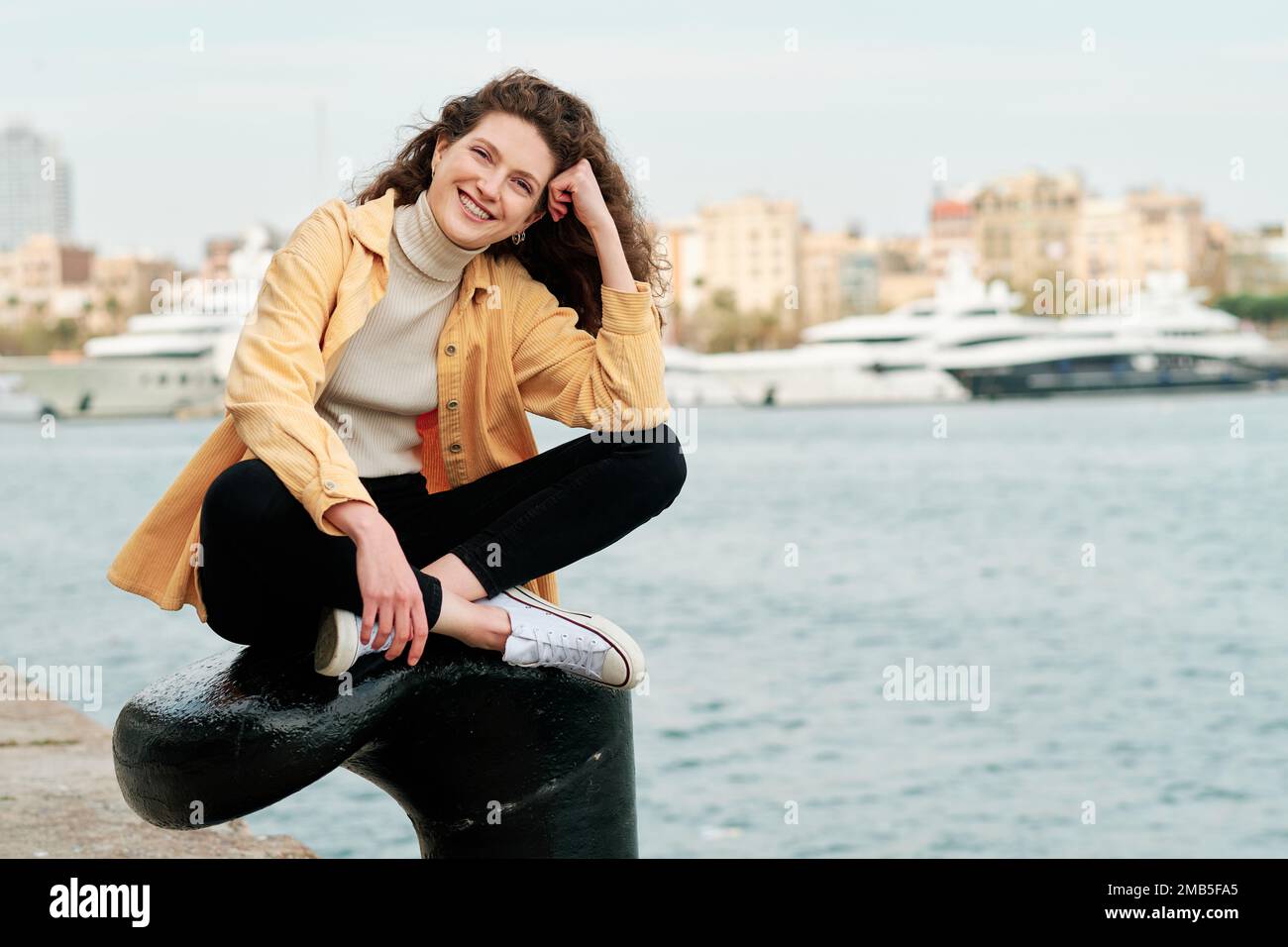 Young woman looking at camera and smiling while posing at the sea ...