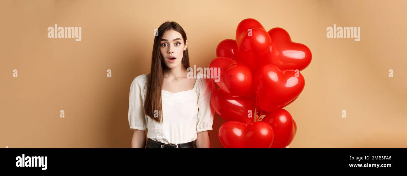 Surprised pretty girl standing near heart balloons and looking with awe ...