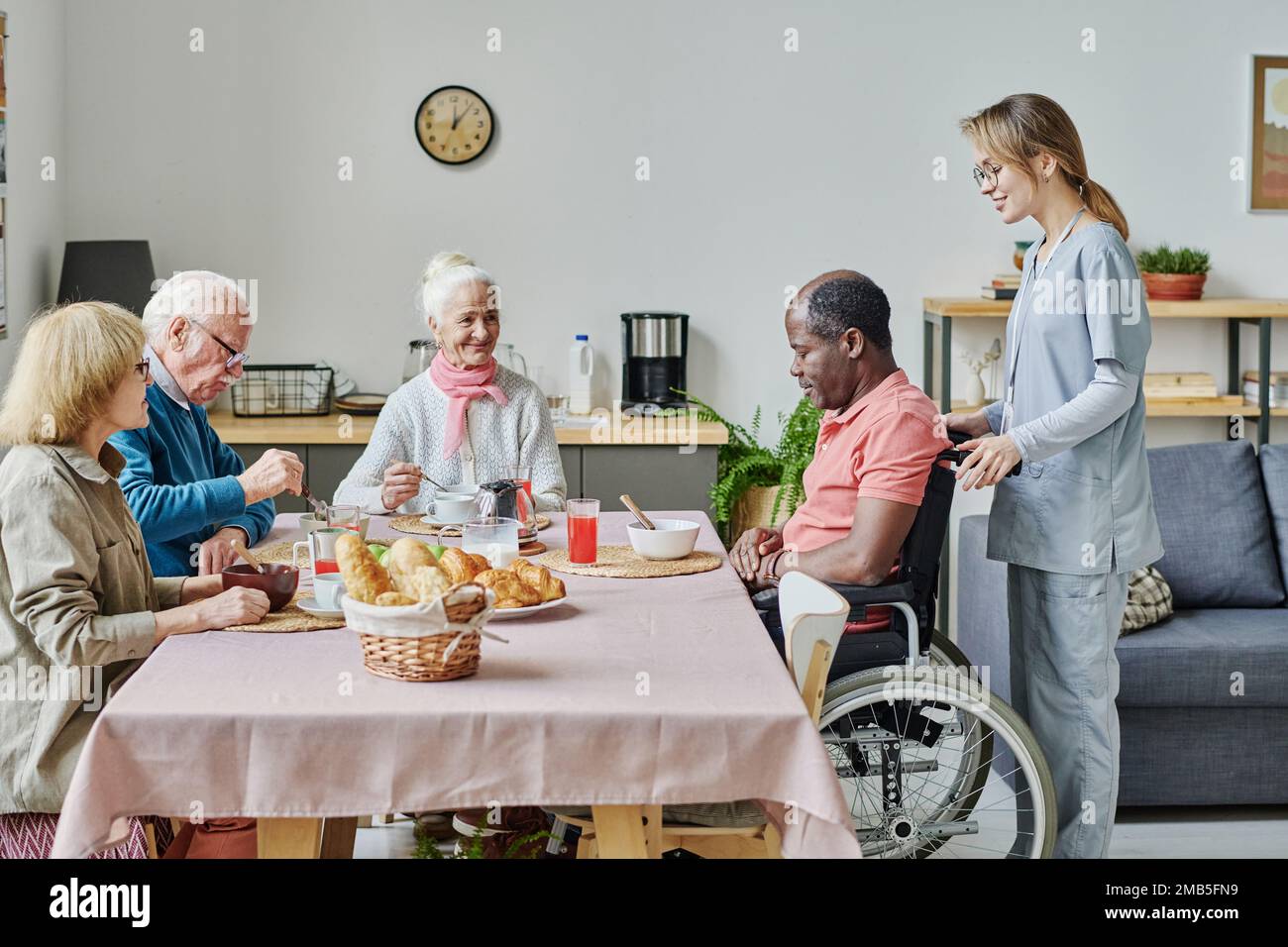 Senior people sitting at table and eating with caregiver helping man ...
