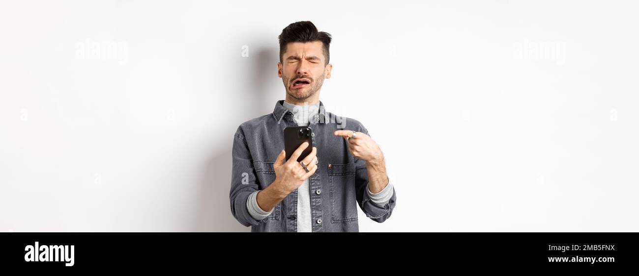 Sad crying guy pointing at smartphone and sobbing, complaining or ...