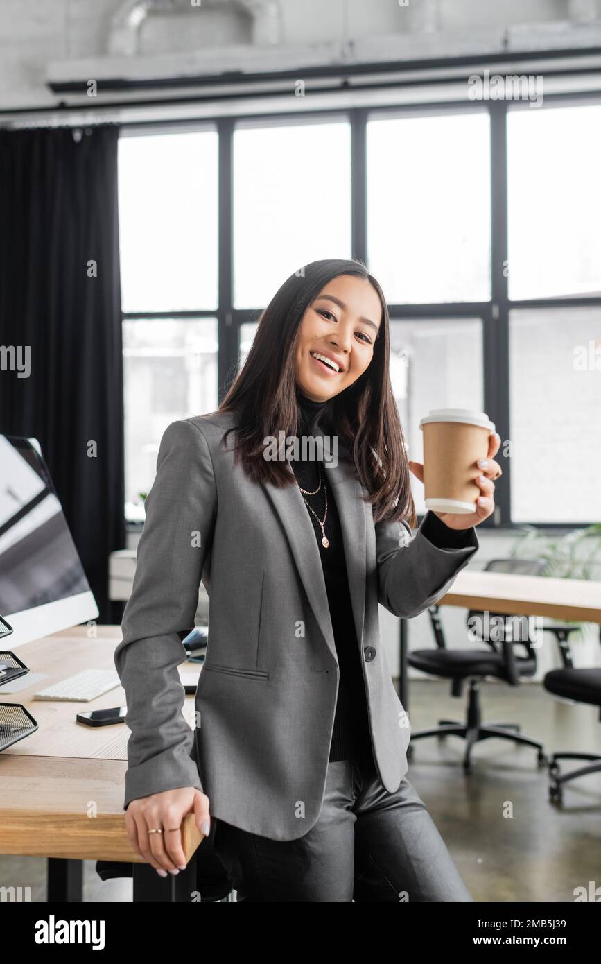 Smiling asian interior designer holding coffee to go in office,stock ...