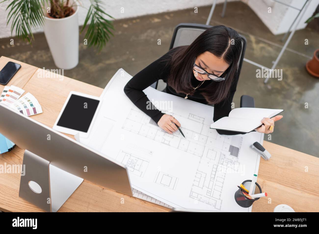 Overhead view of asian designer working with blueprint and notebook in ...