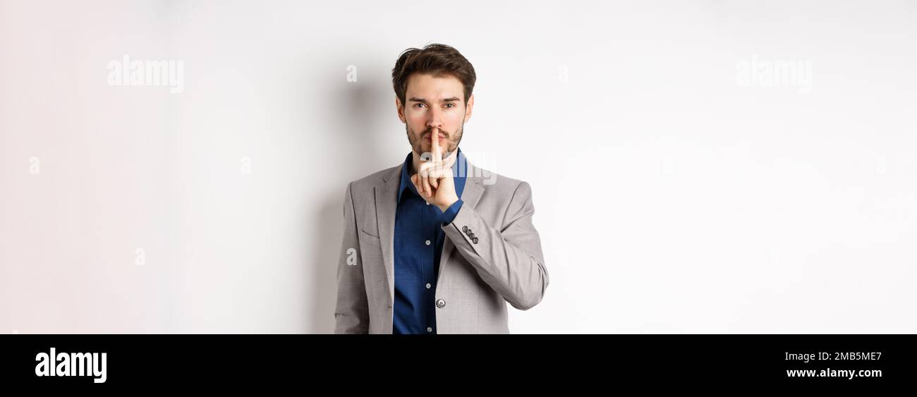 Handsome macho man in suit shushing at camera, press finger to lips ...
