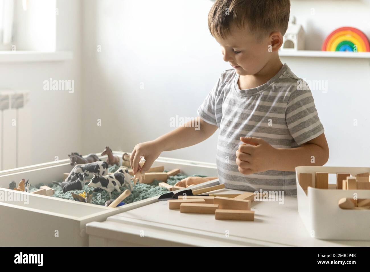 Cute baby boy playing sensory box kinetic sand table with farm animals ...