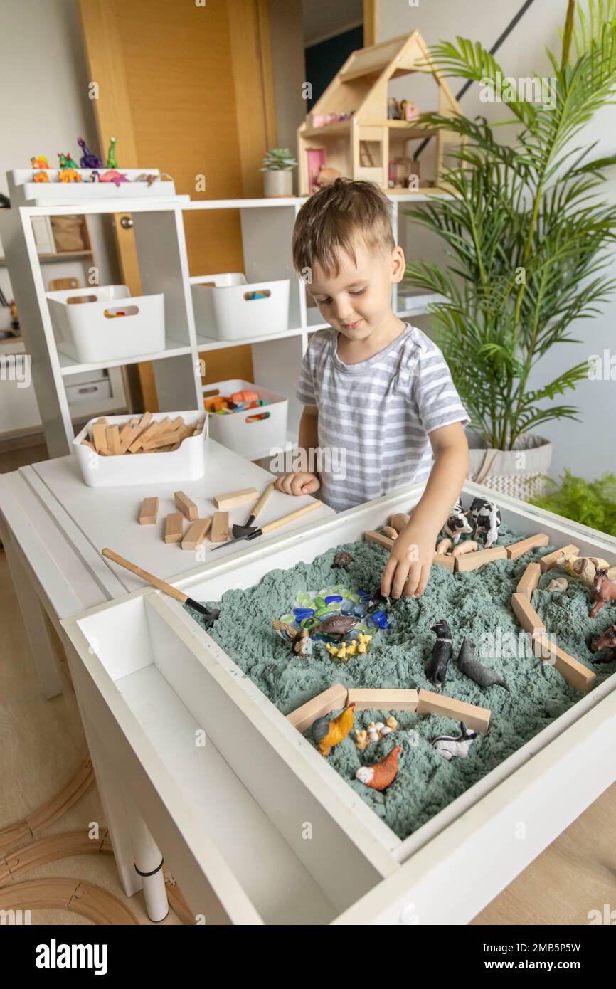 Cute baby boy playing sensory box kinetic sand table with farm animals ...