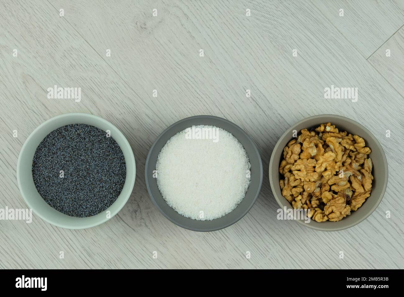 Poppy seeds, coconut shavings and walnut in bowls on a woody background ...