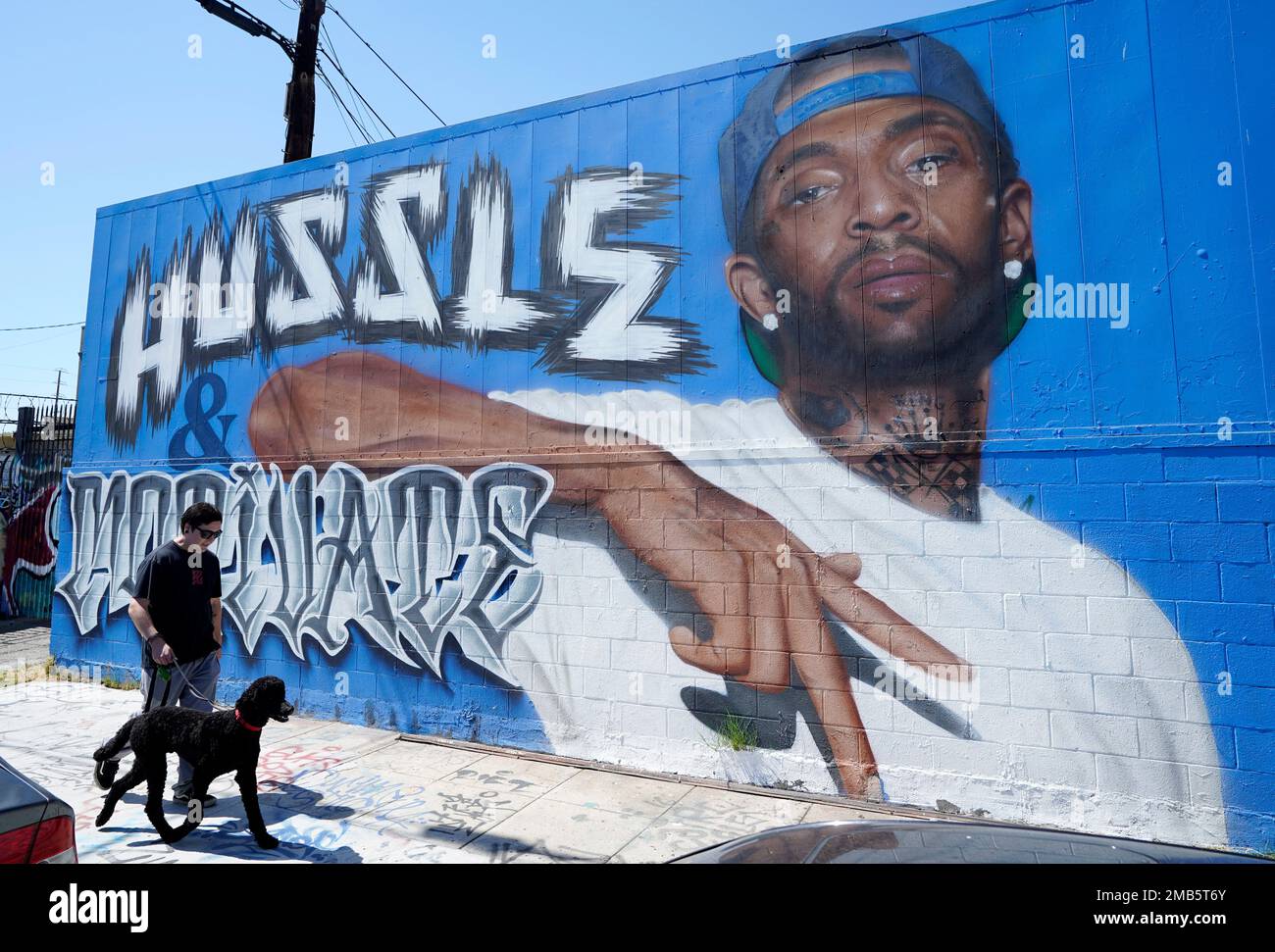 A man walks his dog past a street mural of the late rapper Nipsey ...